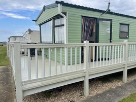 Uma casa móvel verde com deck branco e varanda coberta.