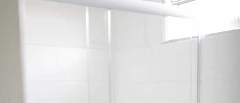 Divisória de chuveiro envidraçada com azulejos brancos, um pequeno compartimento e um chuveiro à vista.