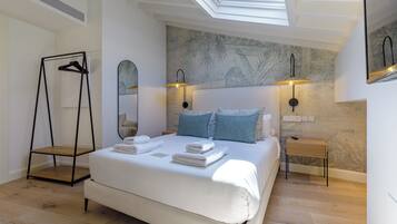 Quarto com cama, um cabideiro, mesa de cabeceira e uma luminária na parede.