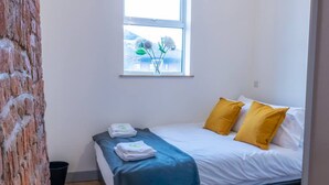 Quarto com cama, janela com vista para flores e parede de tijolos.