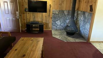Um quarto aconchegante com lareira de pedra, televisão na parede e uma mesa de madeira.