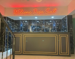 Uma receção com um letreiro de néon que diz "Welcome Paso Suite" e uma exibição com vista para a cidade acima.