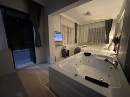 Quarto de hotel moderno com uma banheira grande, uma televisão e uma cama com encosto.