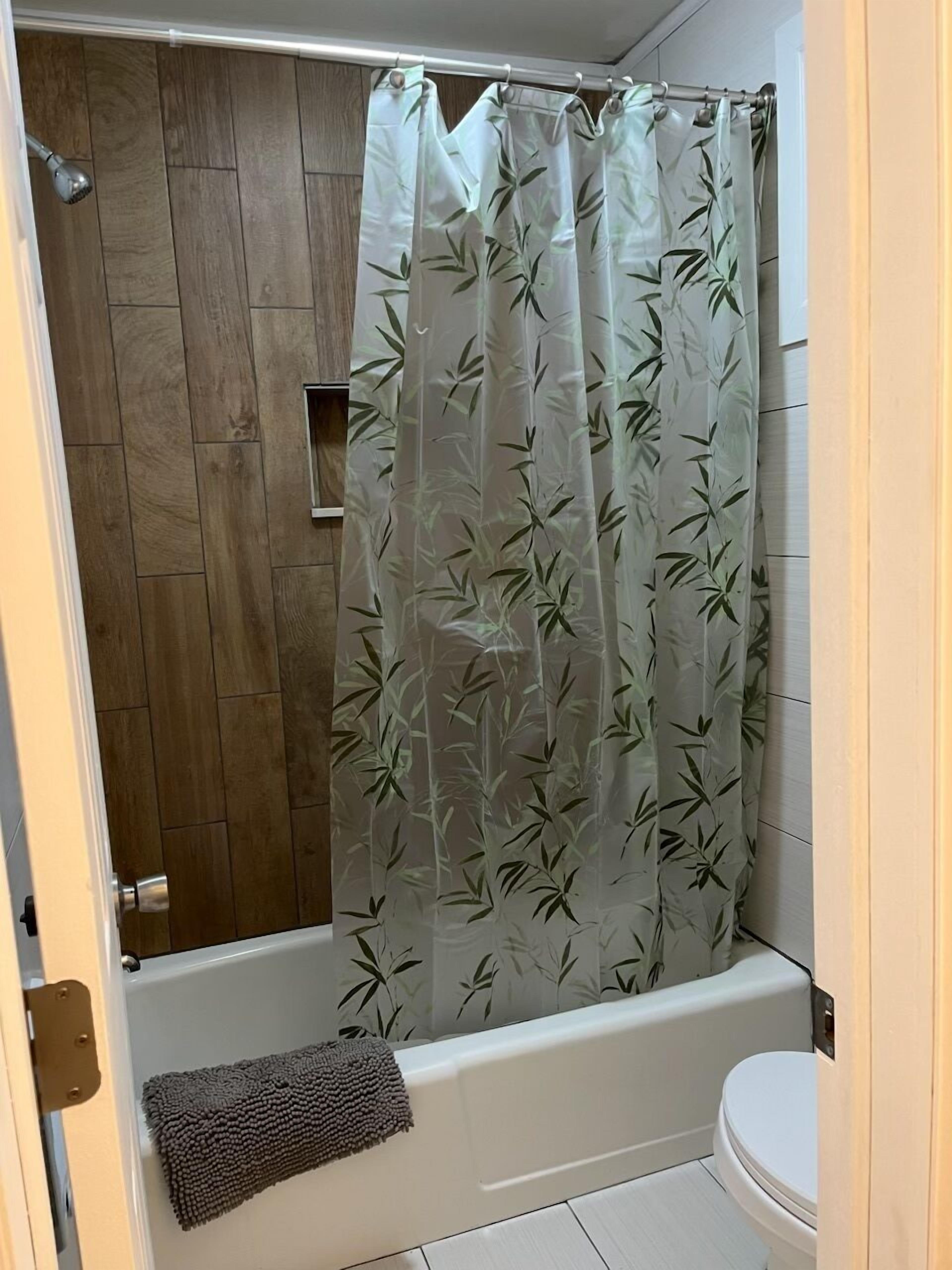 Um banheiro com cortina de chuveiro estampada com bambu, uma banheira e um vaso sanitário.