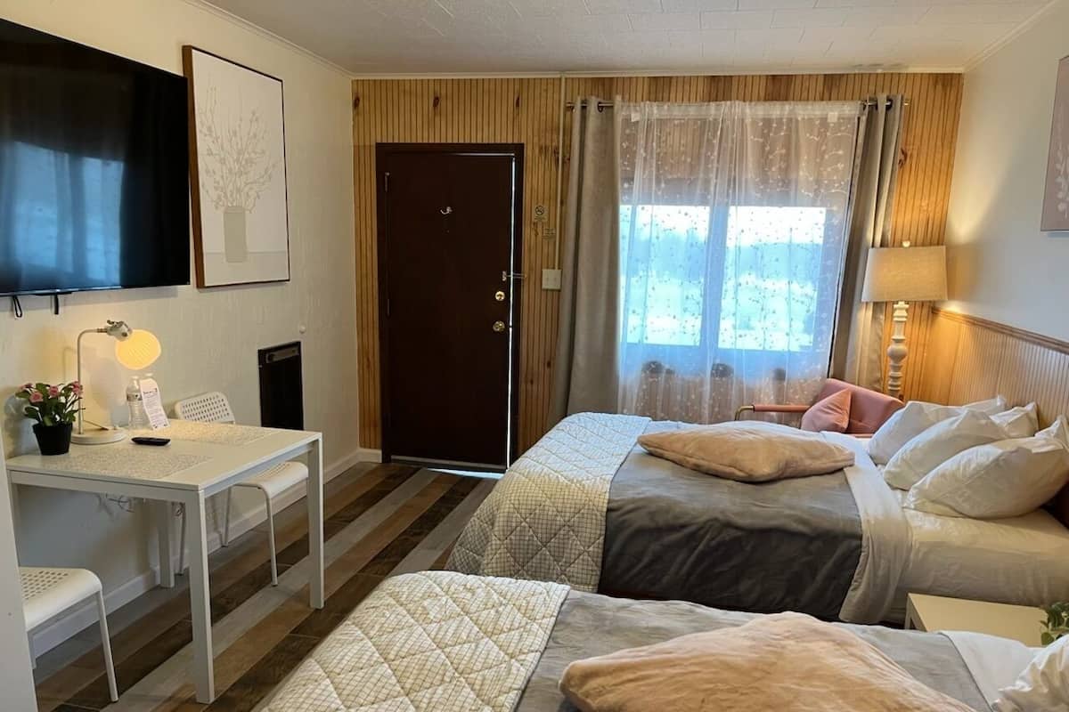 Quarto com duas camas, uma escrivaninha, uma cadeira, uma televisão e uma porta.
