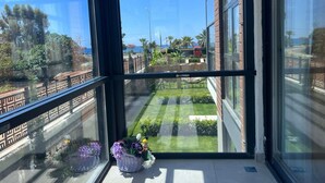 Uma grande janela com vista para um jardim bem cuidado e um edifício ao longe.