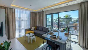 Uma sala de estar moderna com sofá, mesa de centro e área de jantar com vista para palmeiras e edifícios.