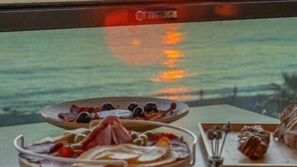 Uma mesa com comida e vista para o pôr do sol sobre a água.
