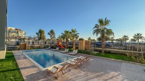 Piscina com espreguiçadeiras, palmeiras e um escorregador.