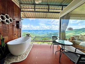 Um banheiro com uma banheira grande, chuveiro e vista para uma paisagem montanhosa.