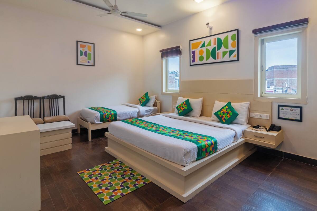 Quarto de hotel com duas camas, uma mesa, uma cadeira e uma janela com vista para a cidade.
