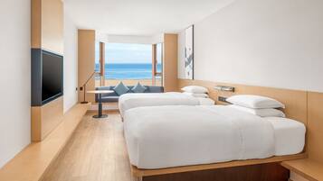 Quarto de hotel moderno com uma cama grande, televisão e vista para o oceano.