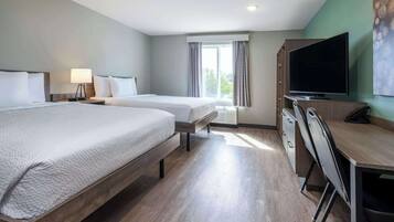 Quarto de hotel com duas camas, uma escrivaninha, uma cadeira, uma televisão e uma janela com cortinas.