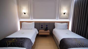 Quarto de hotel com duas camas, mesa de cabeceira com cafeteira e luminárias fixadas na parede.