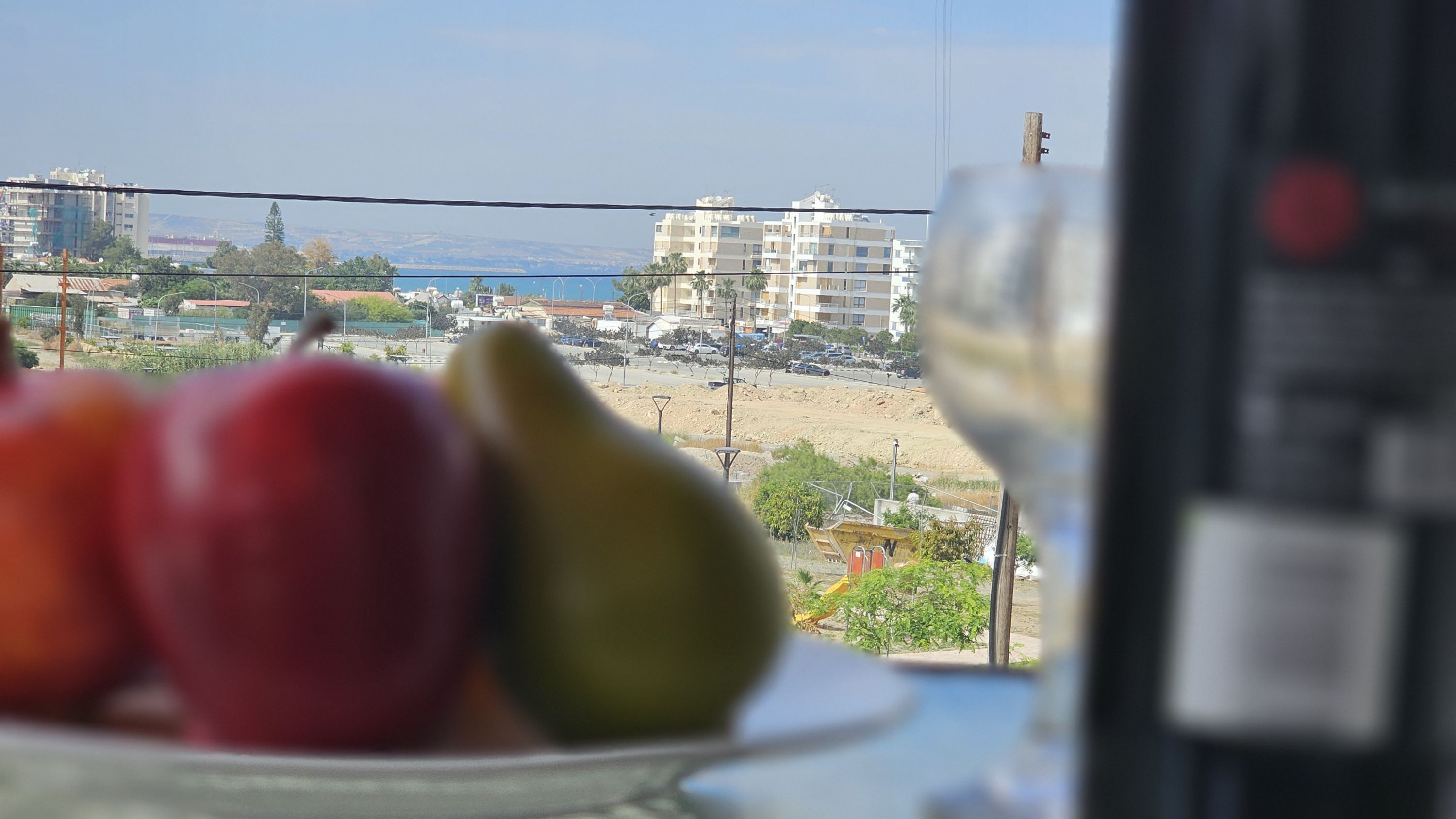 Mesa com uma travessa de fruta e um copo de vinho, com vista para um horizonte urbano com edifícios e uma praia.