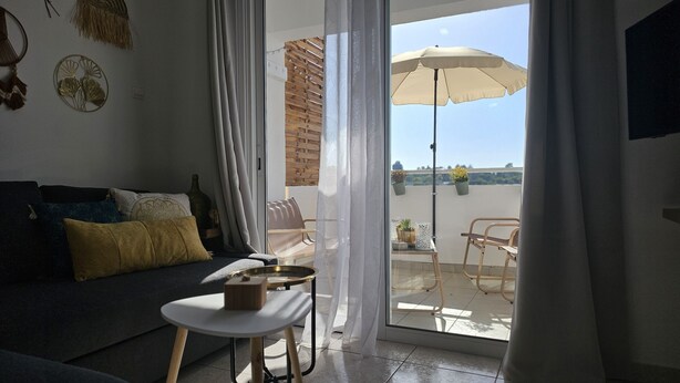 Uma sala de estar com sofá, uma mesa pequena e varanda com guarda-sol.