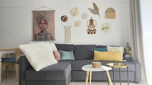 Uma sala de estar moderna com um sofá cinzento, um cobertor branco e uma pequena mesa redonda com base dourada.