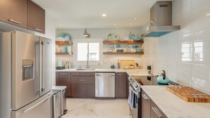 Uma cozinha moderna com eletrodomésticos de aço inoxidável, bancadas de mármore branco e armários de madeira.