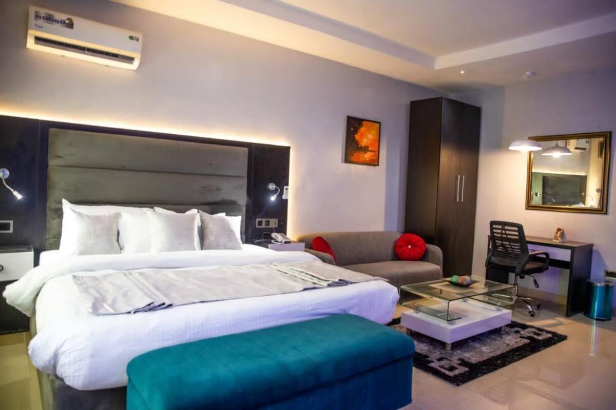 Quarto de hotel moderno com uma cama grande, uma escrivaninha, uma cadeira e um sofá.