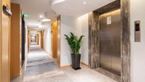 Corredor de hotel com piso de mármore, portas de madeira e um vaso de plantas.