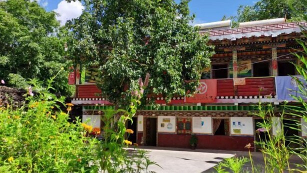 Um edifício tradicional com fachada vermelha e branca, varanda e área de jardim com diversas plantas e flores.