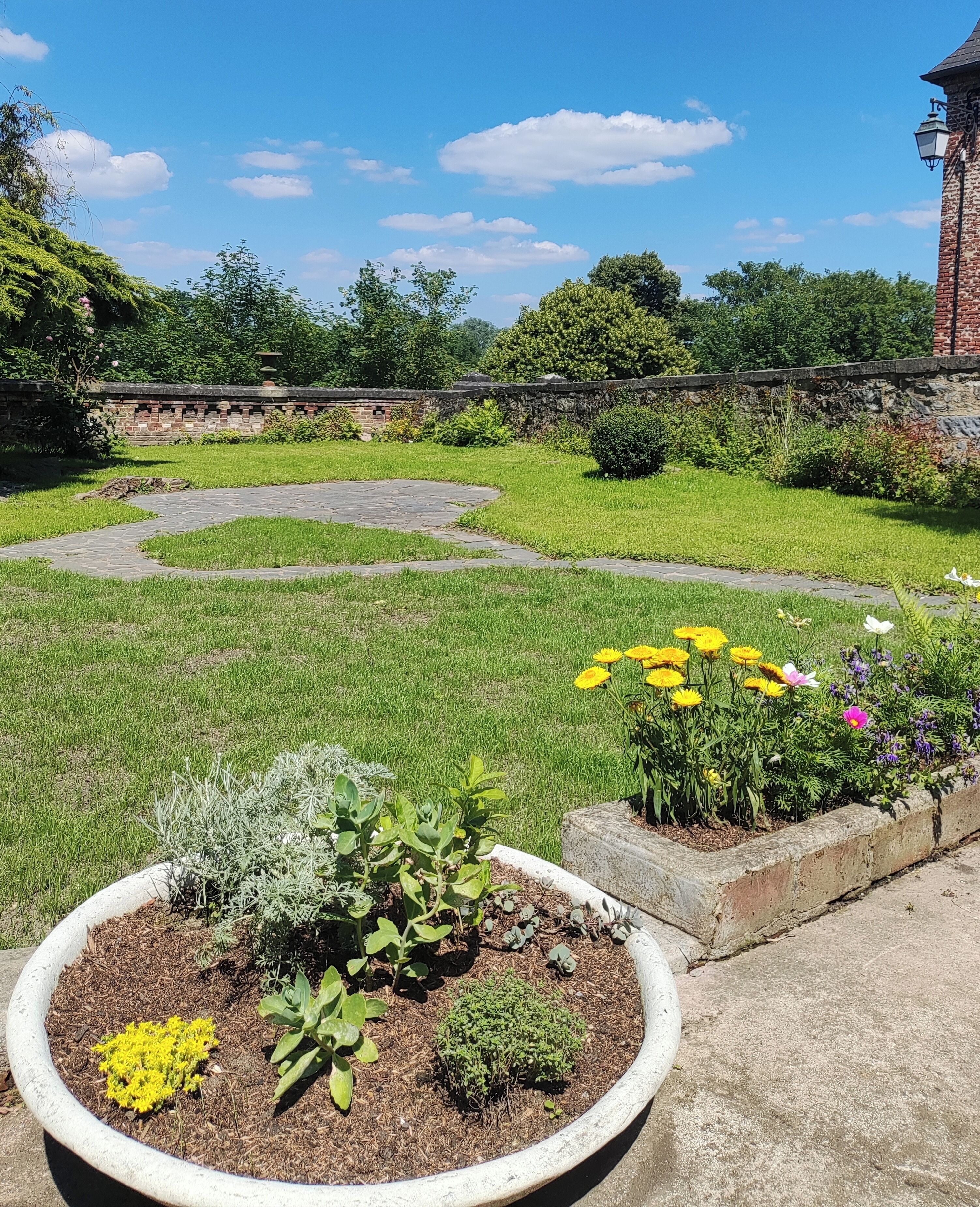 Um jardim ajardinado com caminho de pedra, canteiros de flores e uma parede de tijolos.