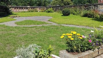 Um jardim ajardinado com caminho de pedra, canteiros de flores e uma parede de tijolos.