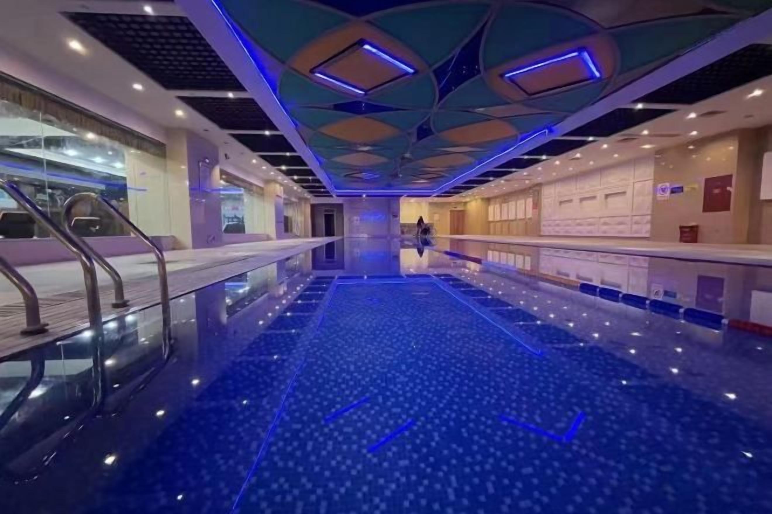 Um saguão de hotel com área de piscina, balcão de recepção e escadaria que leva aos andares superiores.
