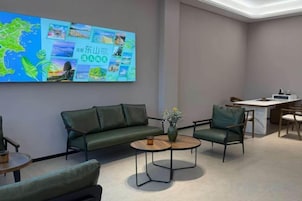 Um lobby de hotel moderno com um conjunto de sofá verde, uma mesa de centro redonda e uma área de refeições com uma mesa e cadeiras brancas.