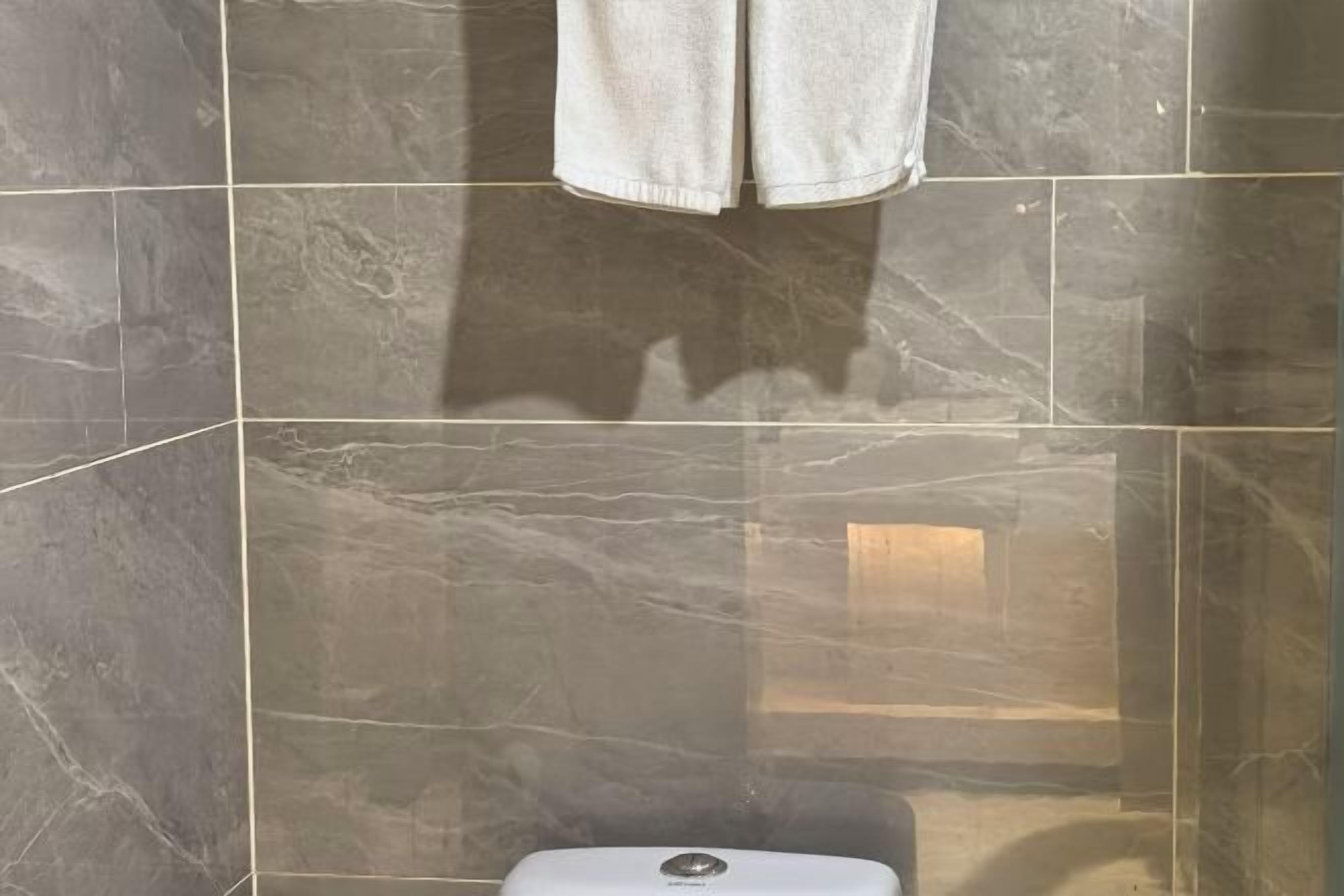 Um banheiro com azulejos de mármore escuro, uma toalha branca pendurada na parede e um vaso sanitário branco.