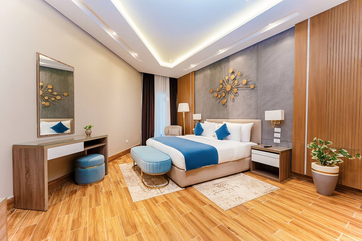 Quarto de hotel moderno com uma cama grande, uma escrivaninha, um espelho com bancada e um vaso de plantas.