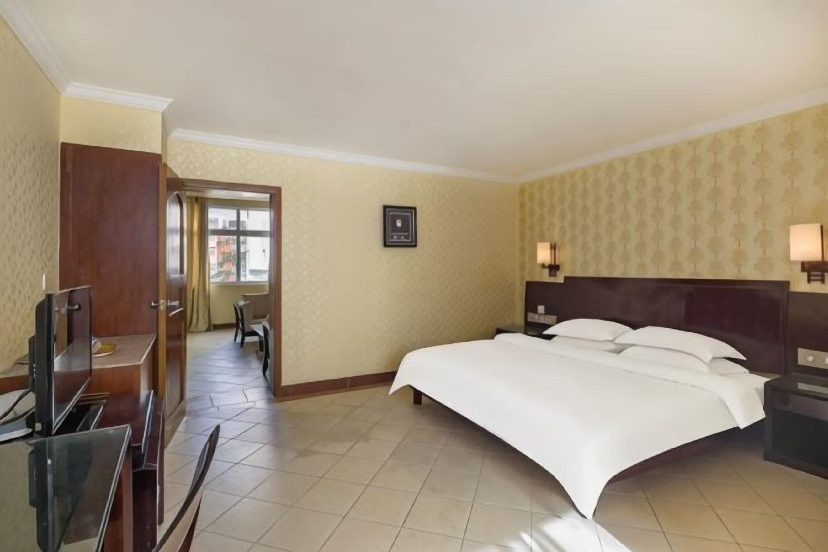 Quarto de hotel com cama, mesas de cabeceira, televisão e escrivaninha.