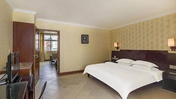 Quarto de hotel com cama, mesas de cabeceira, televisão e escrivaninha.