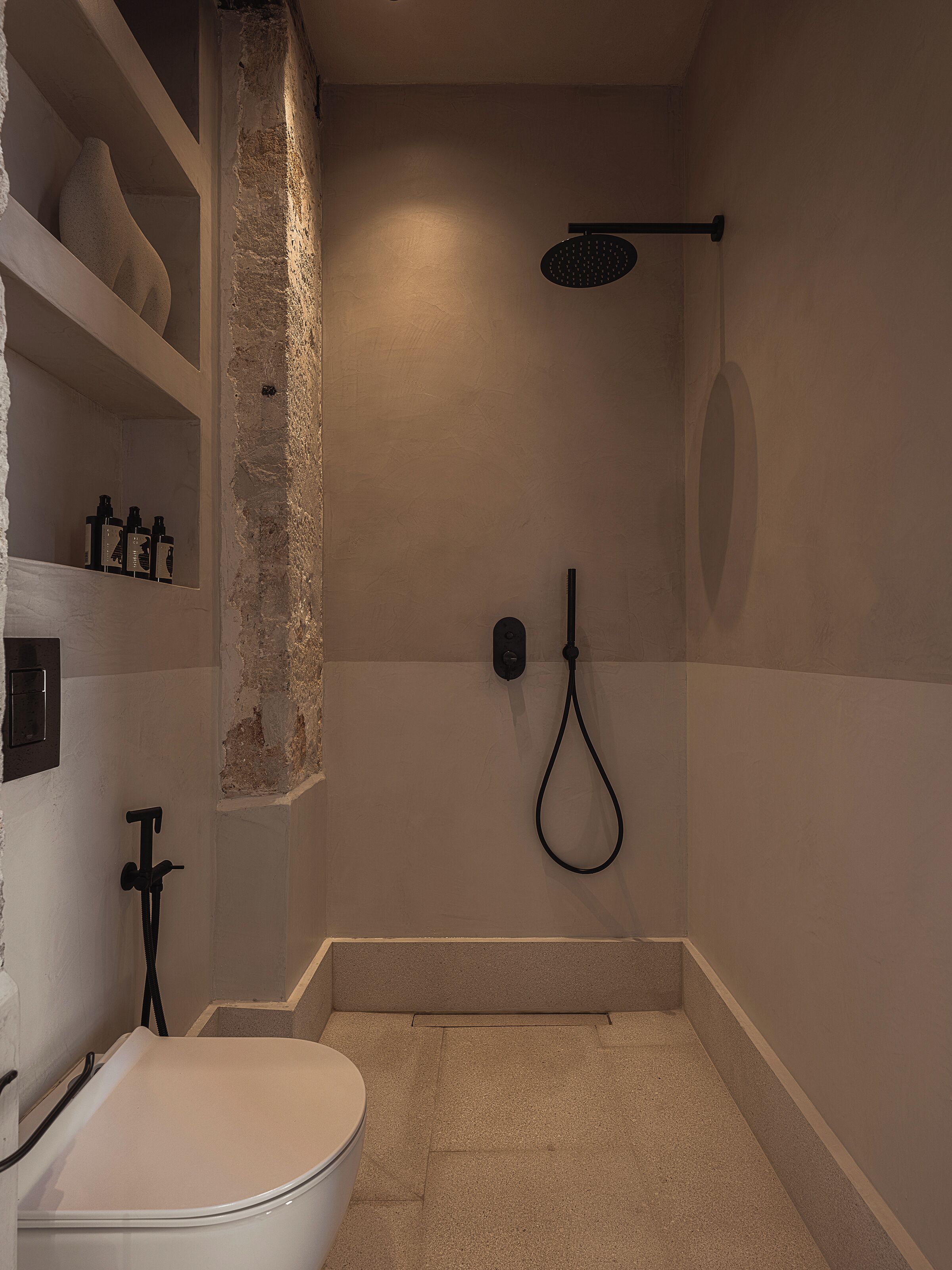 Casa de banho moderna com sanita, chuveiro e prateleiras com artigos de higiene pessoal.