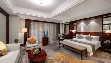Quarto de hotel com cama, sofá, mesa de centro, televisão e um espelho grande.