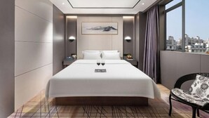 Quarto de hotel moderno com uma cama grande, vista para a cidade e um espaço de refeições com uma cadeira.