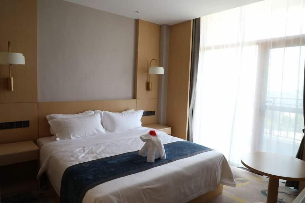 Quarto de hotel com cama, mesas de cabeceira, uma mesa redonda e uma janela com cortinas.