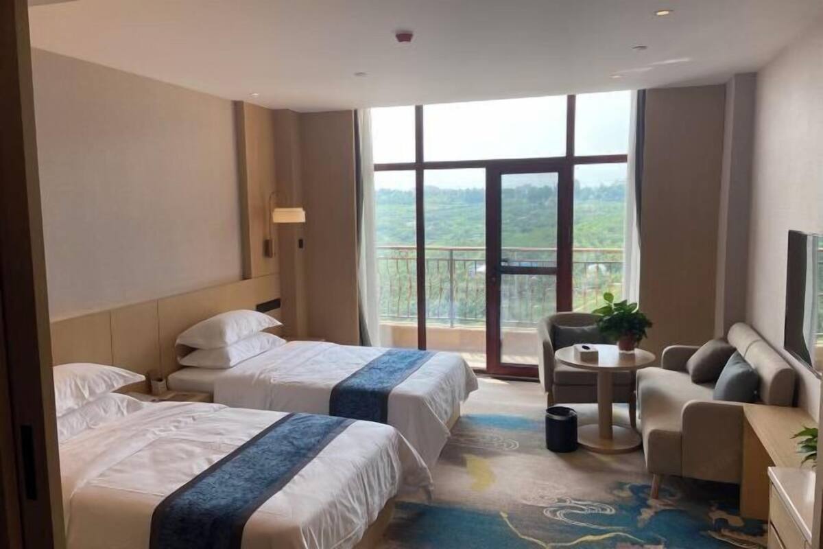 Quarto de hotel com duas camas, um sofá, uma mesinha e uma varanda com vista.