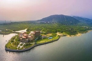 Hotel na ilha com um edifício grande, rodeado por água e vegetação, e montanhas ao fundo.
