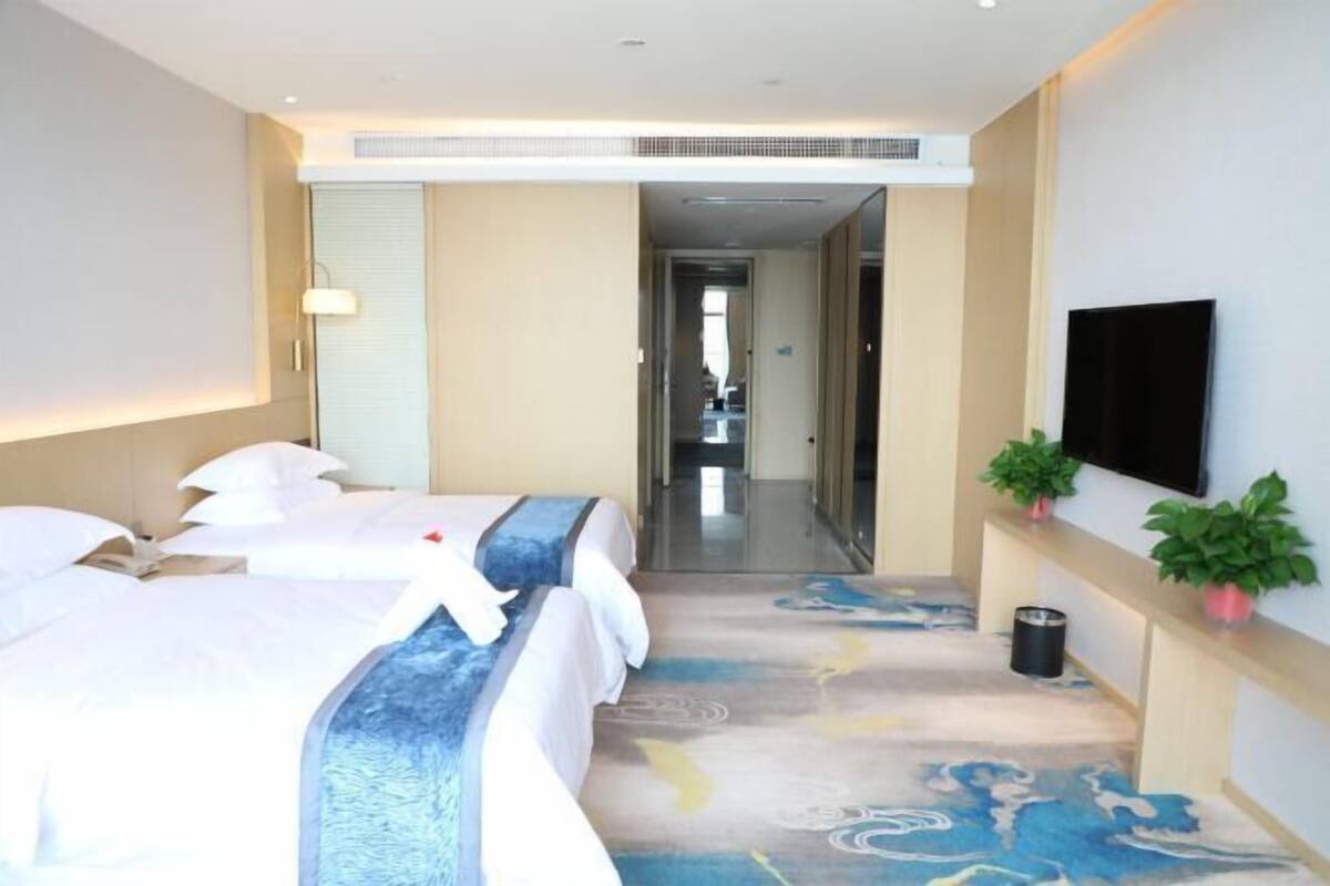 Quarto de hotel com cama, televisão, espelho e corredor que dá para um banheiro.