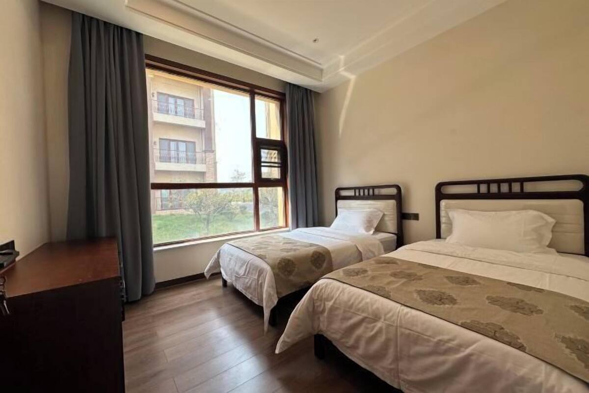 Quarto de hotel com duas camas, uma mesa e uma janela com cortinas.