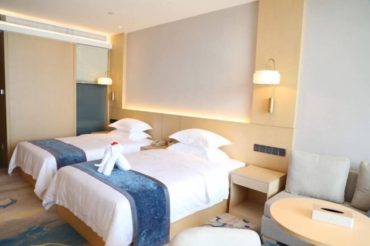 Quarto de hotel com duas camas, uma mesa de cabeceira, uma cadeira, uma mesa redonda e um espelho grande.