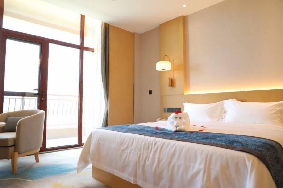 Quarto de hotel com cama, poltrona, mesa de cabeceira, luminária e vista para o exterior.
