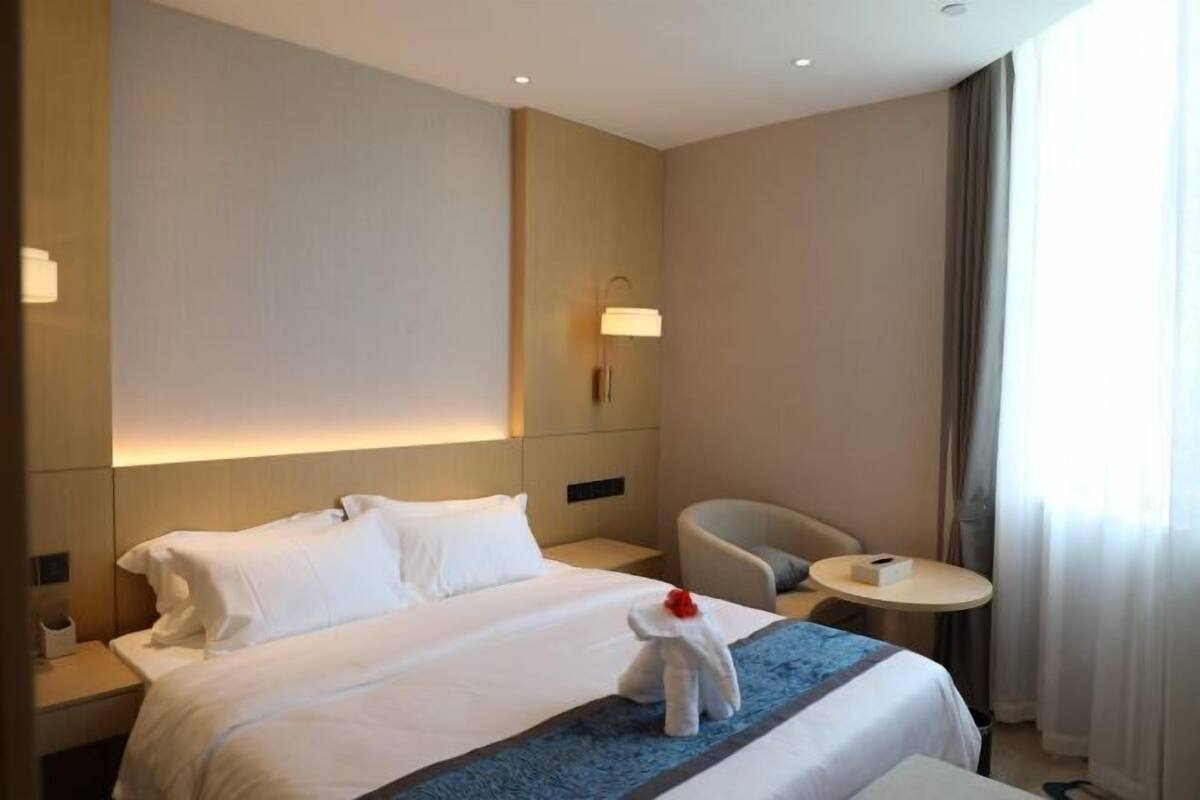 Quarto de hotel com cama, uma cadeira, uma mesinha e uma luminária.