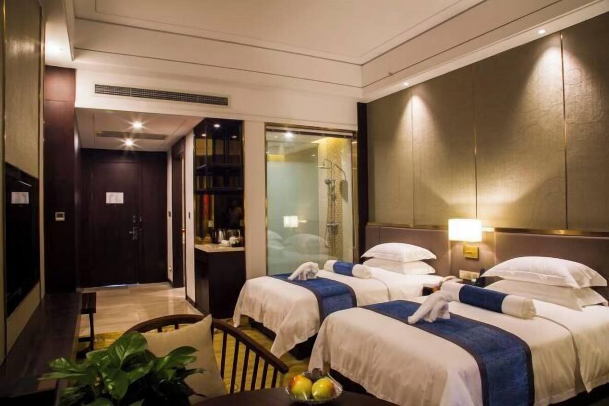 Quarto de hotel com duas camas, uma escrivaninha e uma mesinha com frutas.