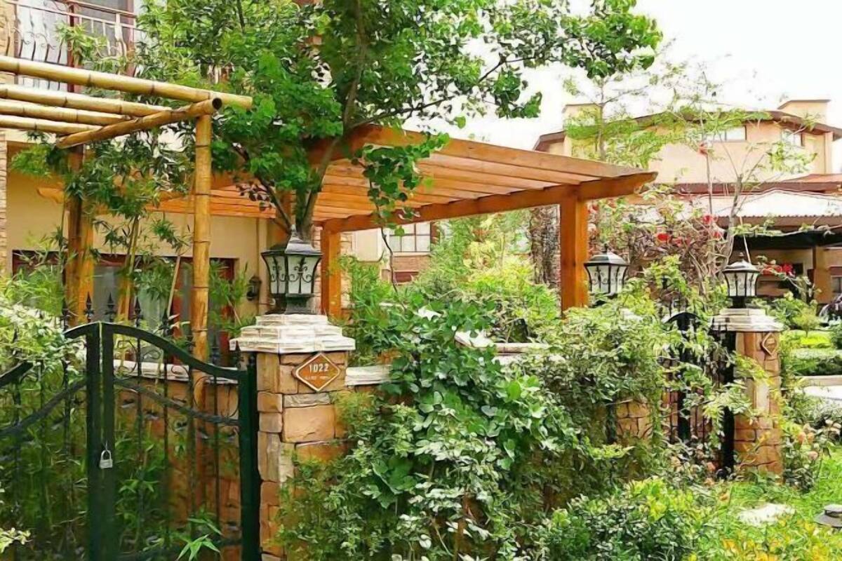 Um jardim com pérgola de madeira, pilares de pedra e portão de metal.