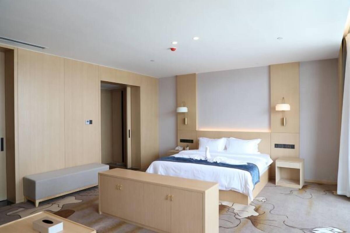 Quarto de hotel com cama, mesas de cabeceira, guarda-roupa e um banco.