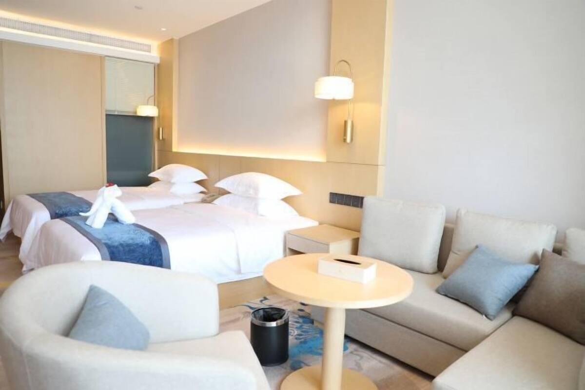 Quarto de hotel com cama, duas mesas de cabeceira, uma mesa de centro redonda, um sofá e uma poltrona.