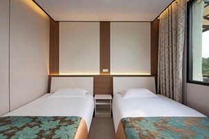 Quarto de hotel com duas camas, uma mesa pequena e uma janela com cortinas.