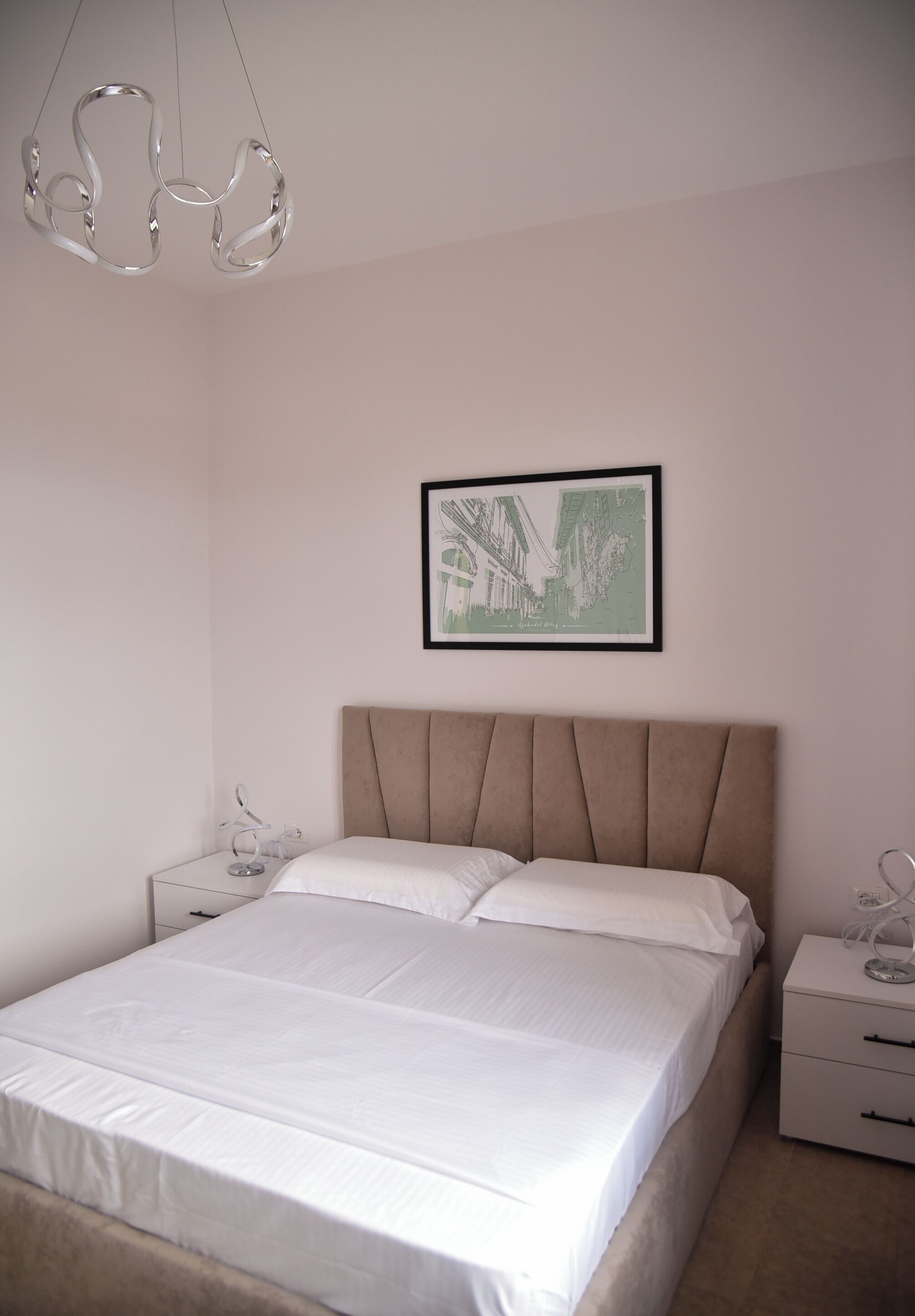Quarto com cama, mesa de cabeceira, luminária pendente e quadro na parede.